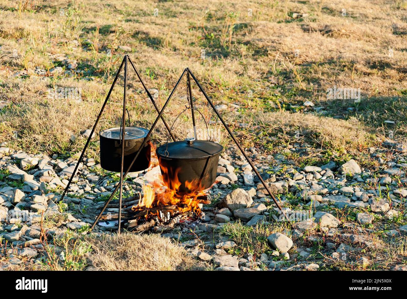 Pair of cook-kettles hanging on tripods over a campfire on nature ...