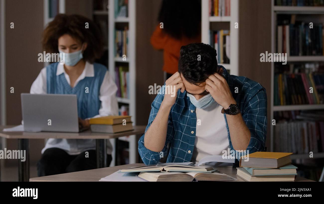 Tired overworked young arab male student in protective mask sits at ...