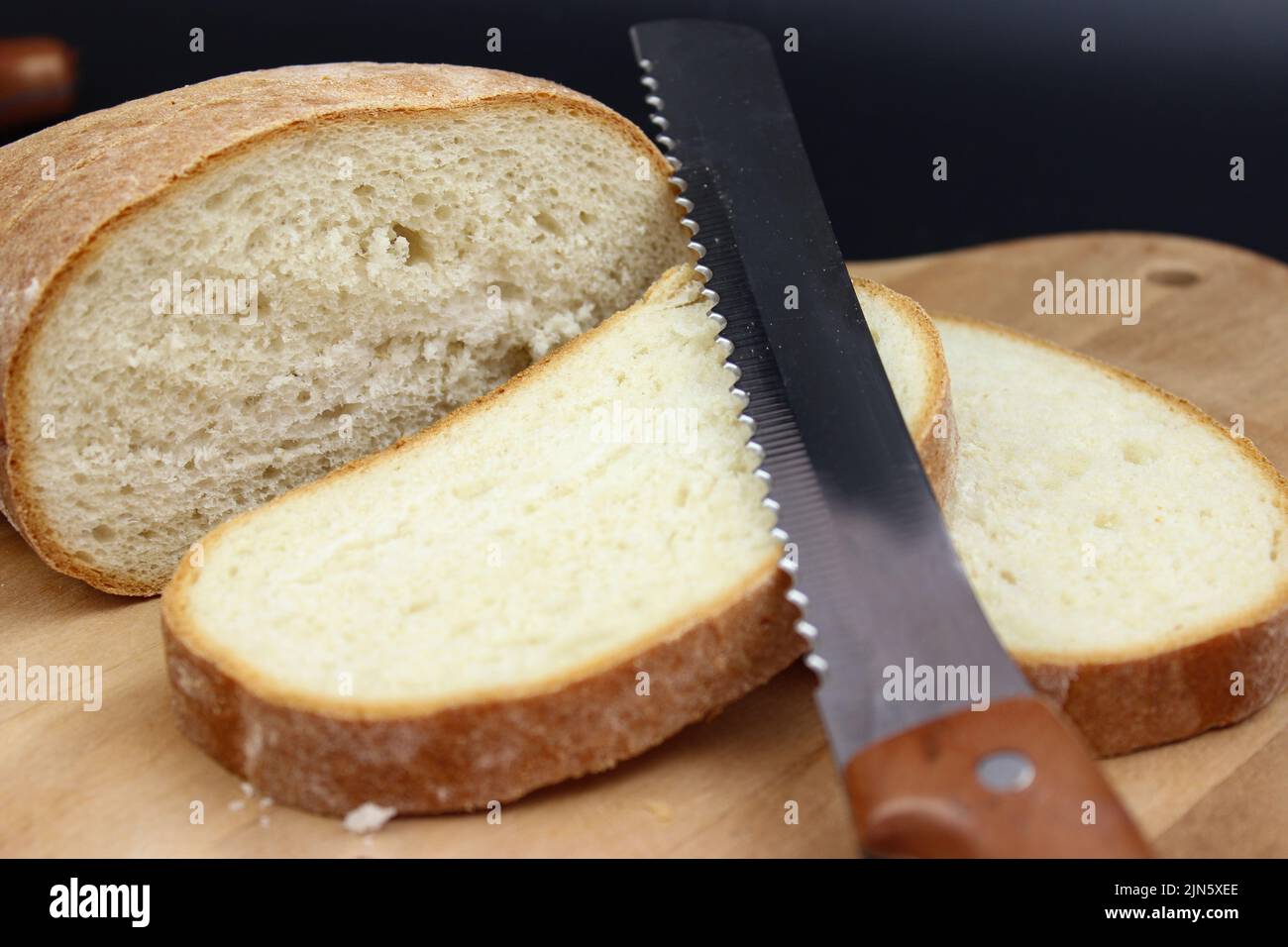 A large knife cuts thin pieces of white bread from a rectangular loaf ...