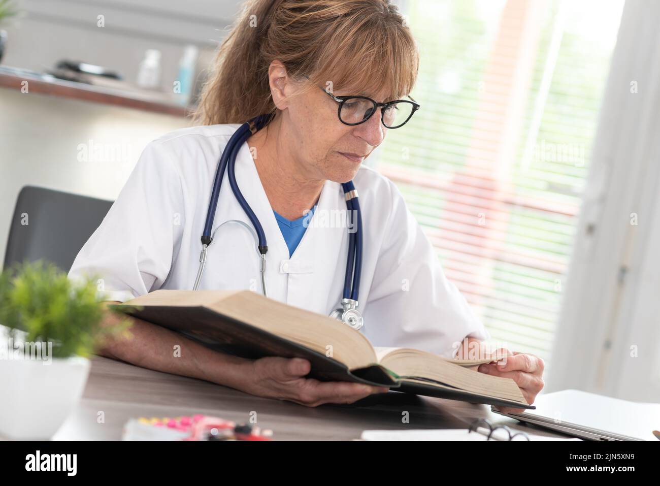 Female doctor reading a textbook in medical office Stock Photo - Alamy