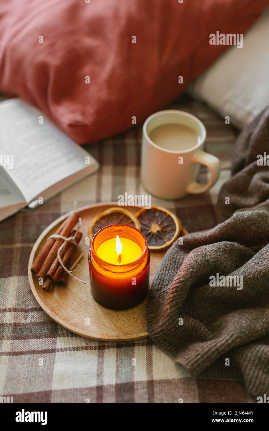 Burning candle with wooden wich in amber glass gar, open book and cup ...