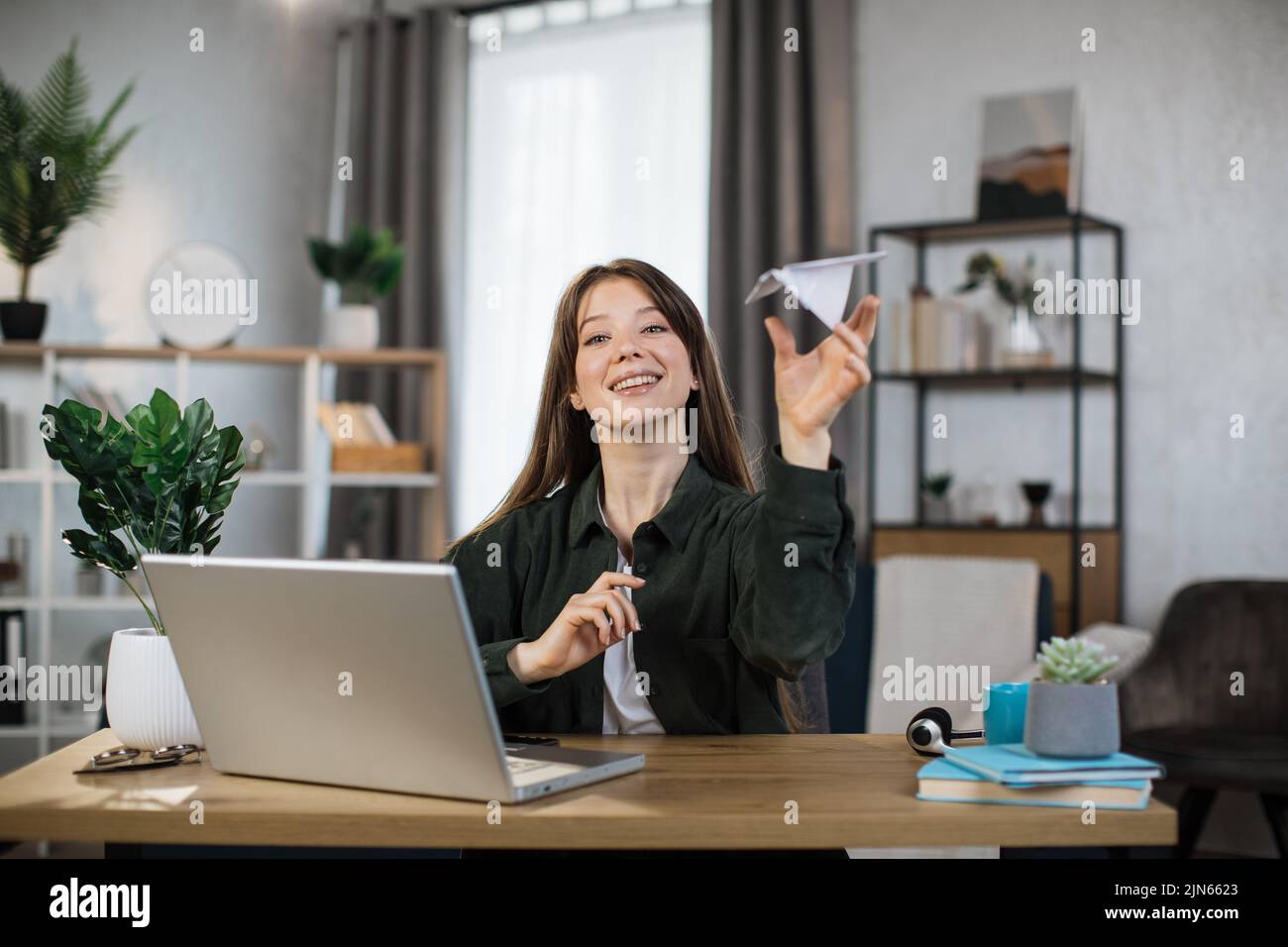 Smiling female freelancer playing with paper plane while working from ...