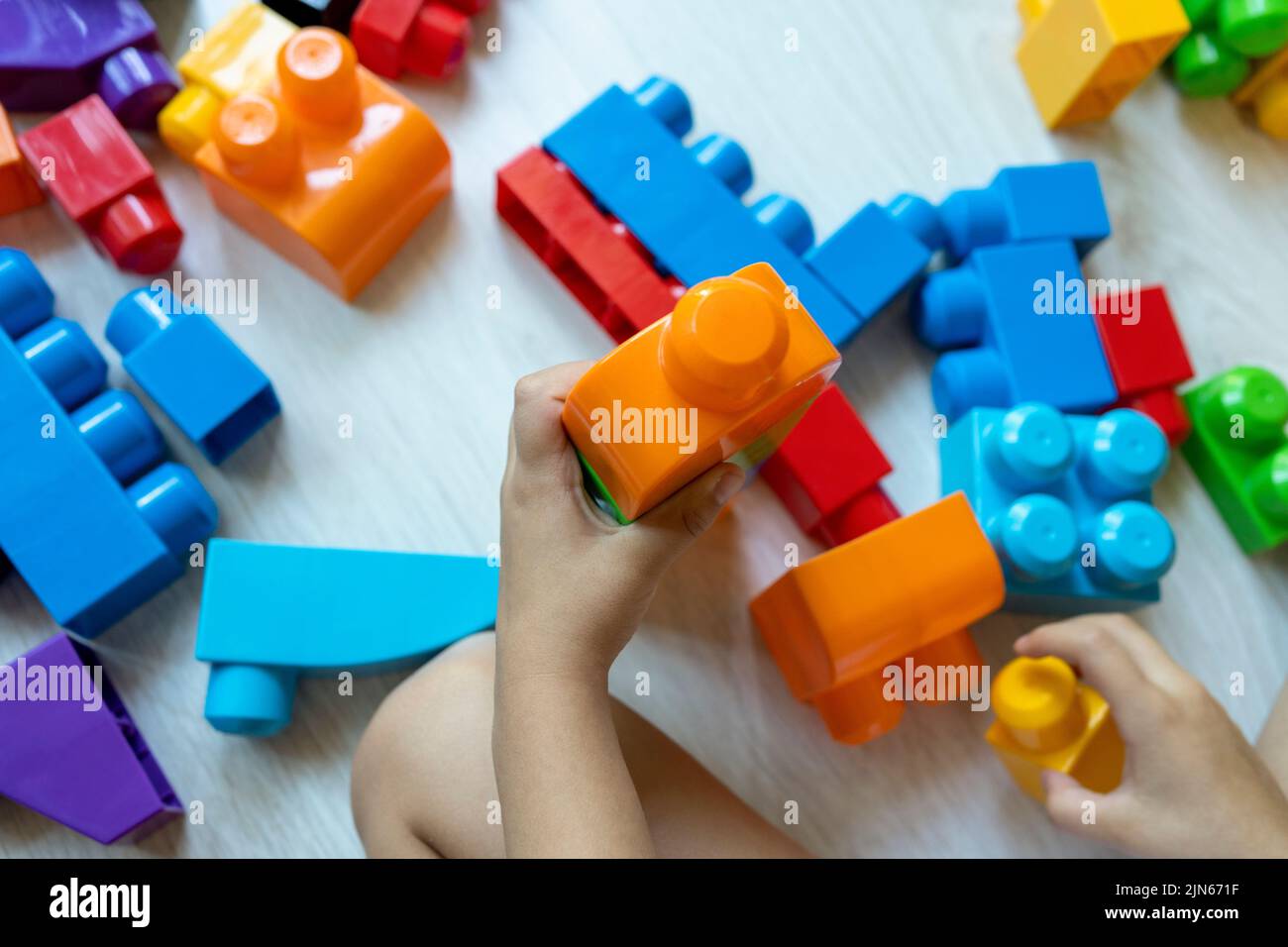 Little boy building tower of block toys sitting on floor in sunny white ...