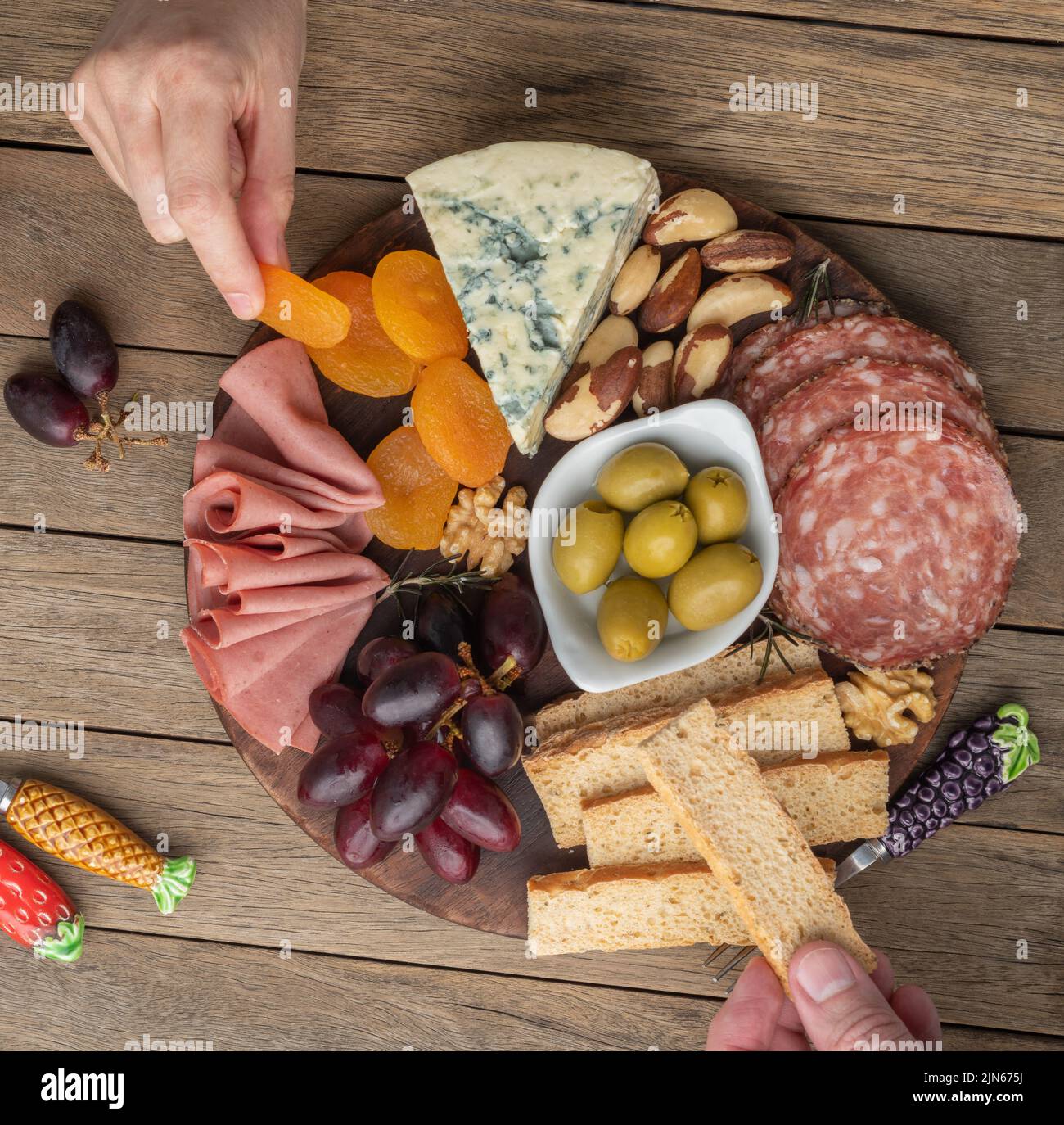 People taking food from appetizer board with cheese, nuts, fruits ...