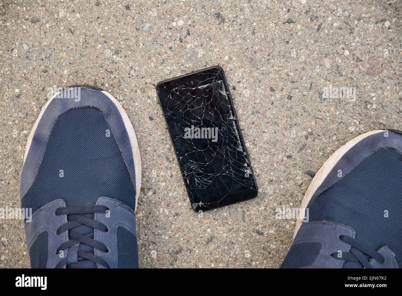 Black smartphone with broken display near the feet of a person on the ...