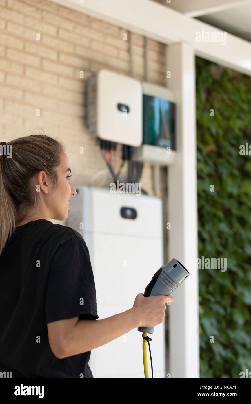 Vertical side view of young woman with a electric car socket on hand ...