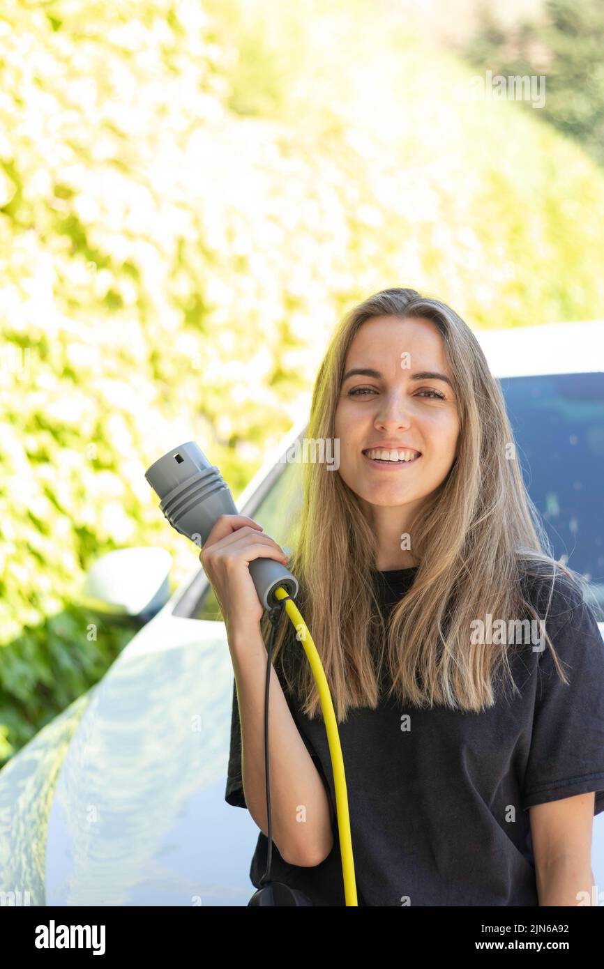 Vertical view of young beautiful woman smiling holding electric car ...
