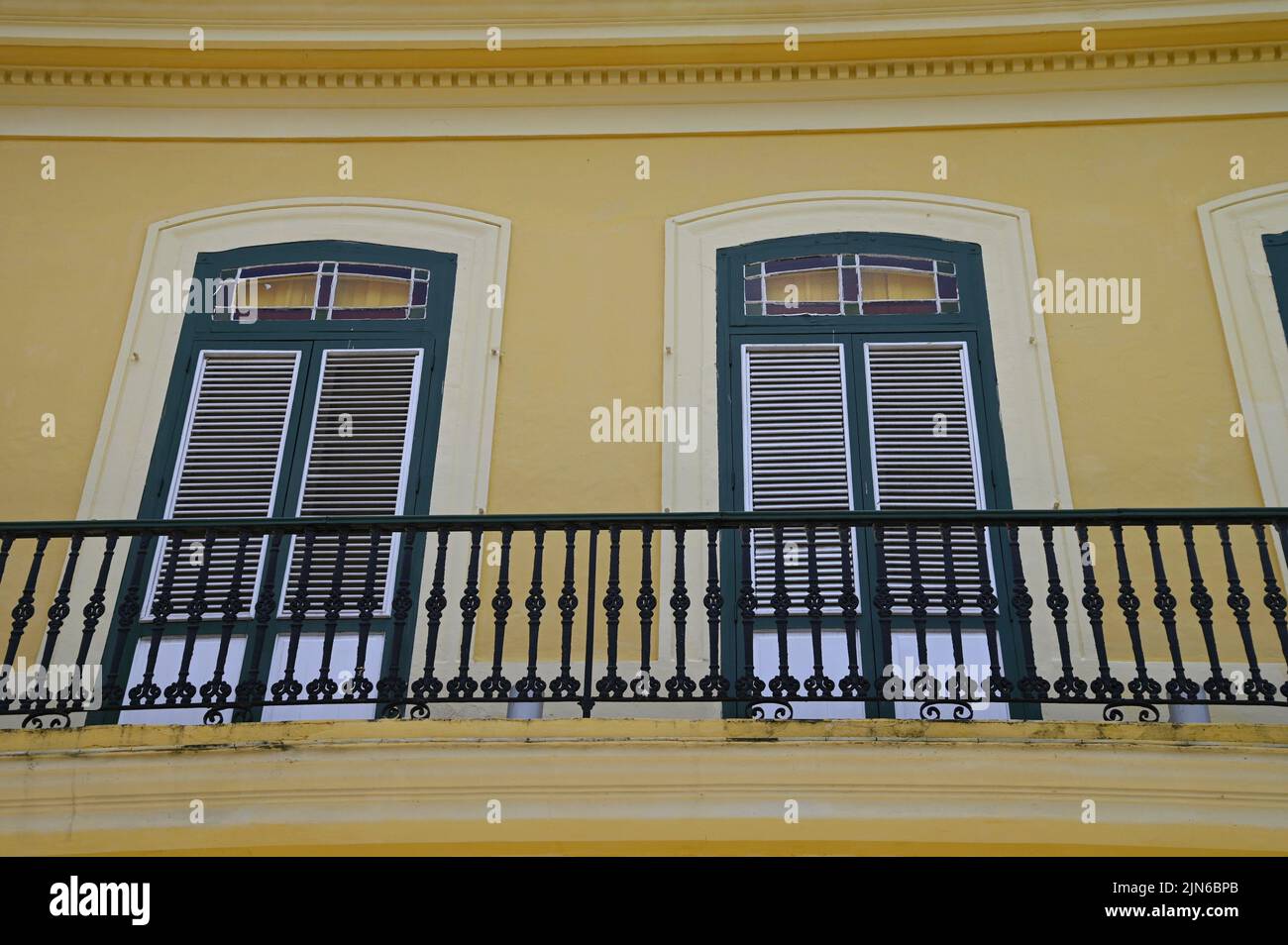 Old Neoclassical building facade with a yellow stucco wall, green ...