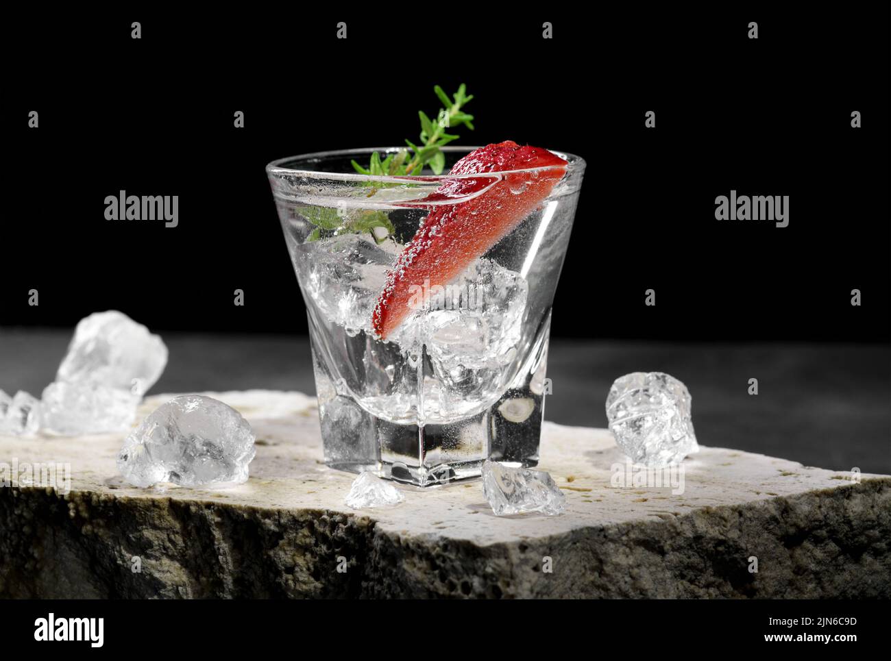 Vodka in shot glass with ice, decorated with strawberry slice and thyme ...