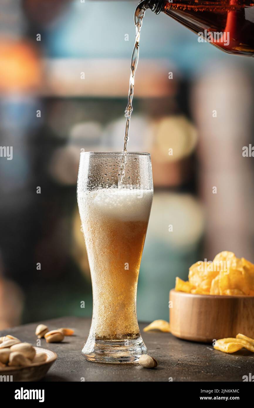 Pouring light foamy beer into glass in bar background. Traditional ...