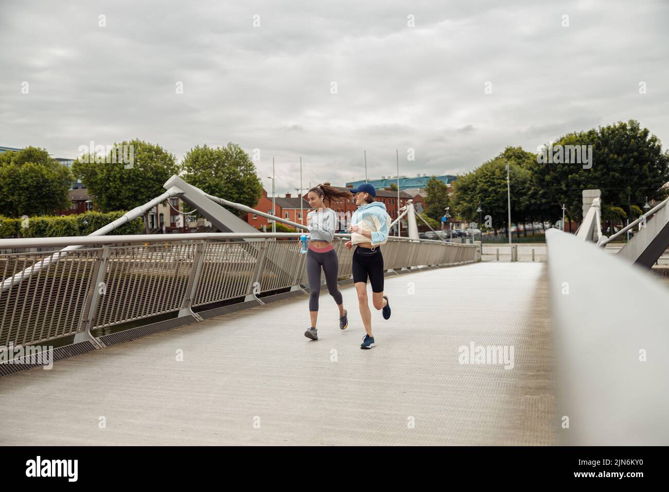 Two athletic women in sportswear is jogging on a bridge and listening ...