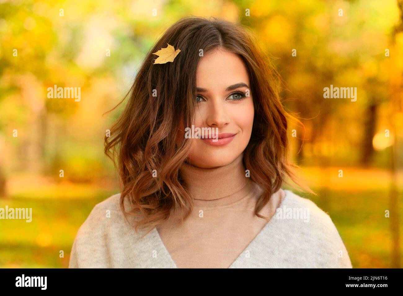 Autumn woman with fall yellow leaf in her hair on gold sunny background ...