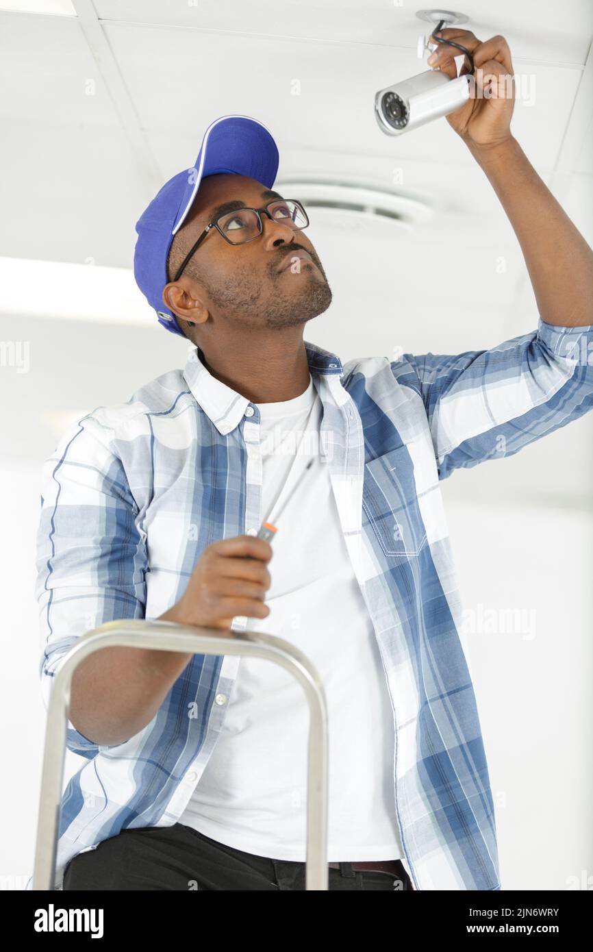 young happy male technician on ladder repairing surveillance camera ...