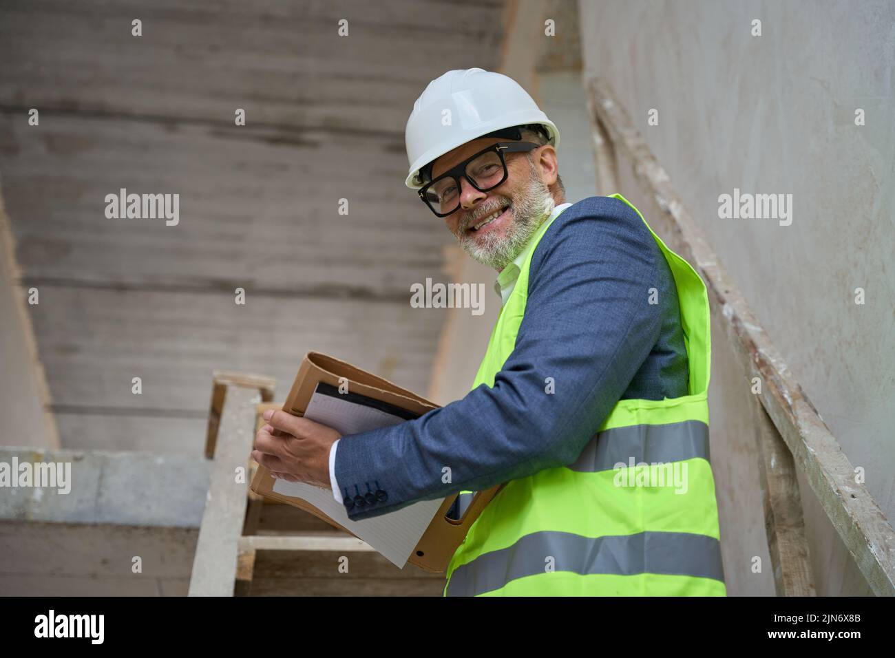 Smiling man foreman holding folder while standing on stairs in cottage ...