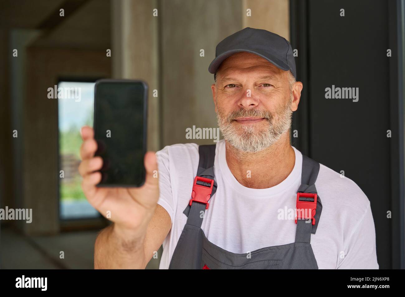 Adult builder in overalls and baseball cap shows phone Stock Photo - Alamy