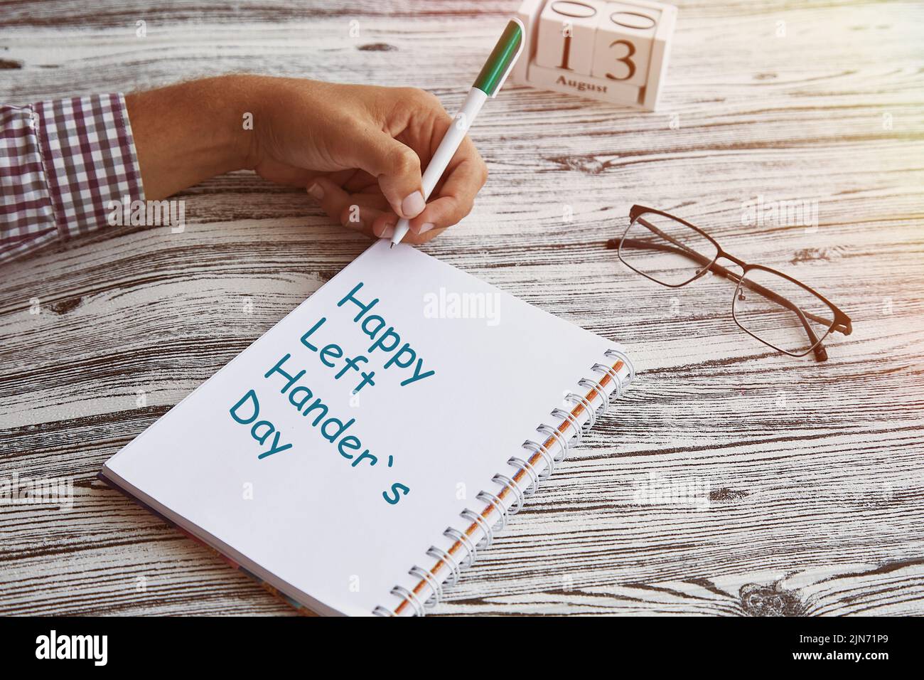 Man uses his left hand to wright in a notebook. Glasess and calendar ...