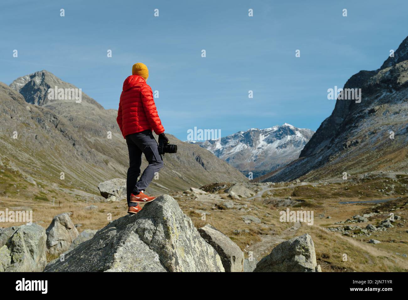 Back view of a tourist man in red jacket and camera standing with a ...