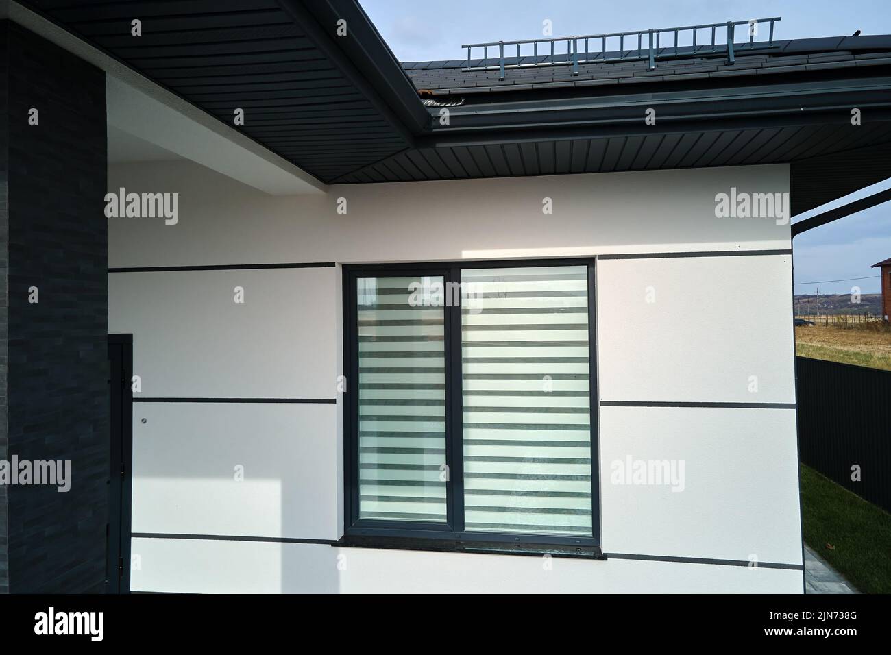 Corner of modern house with shingled roof and big window with closed ...