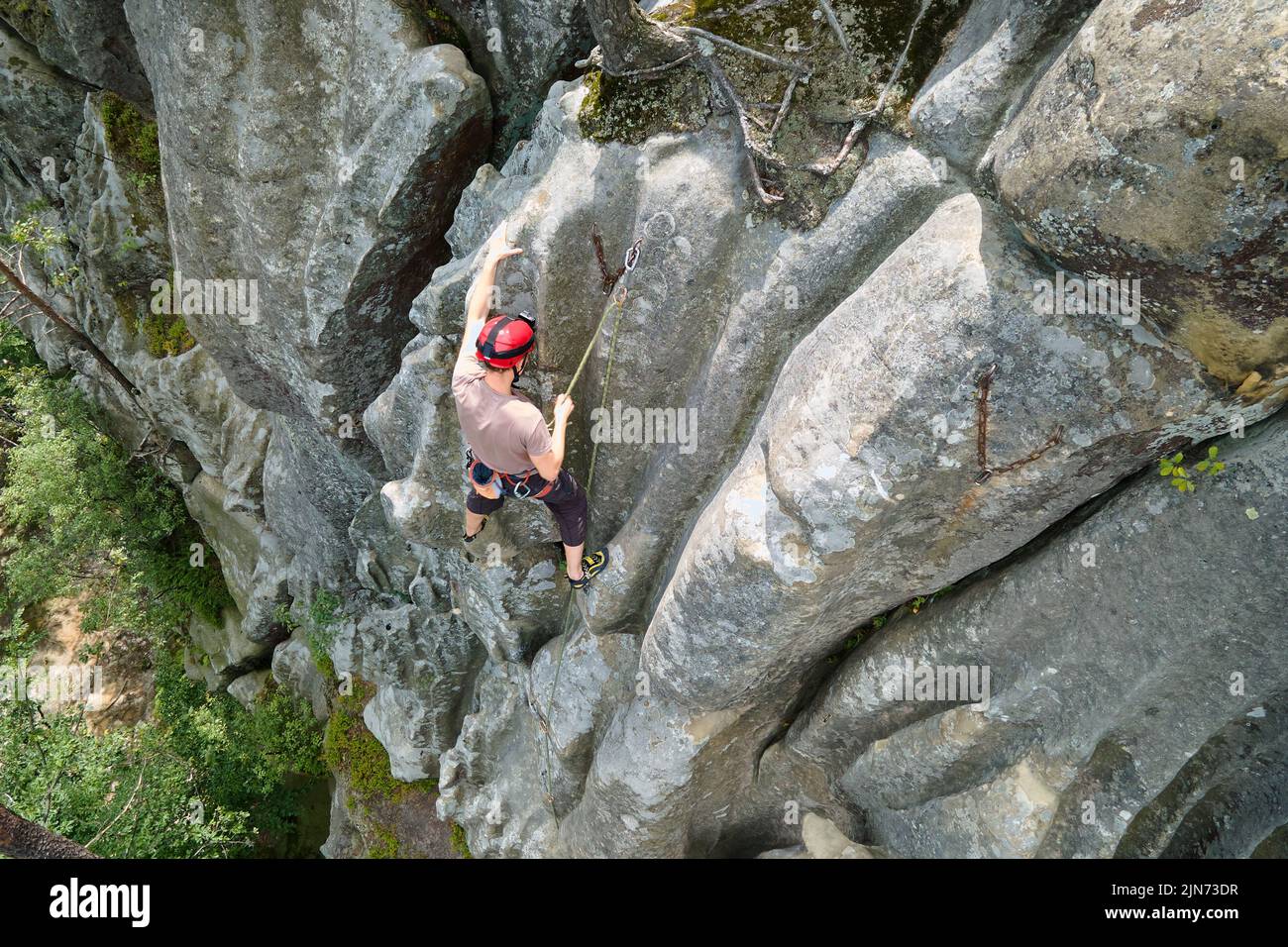 Determined climber clambering up steep wall of rocky mountain ...