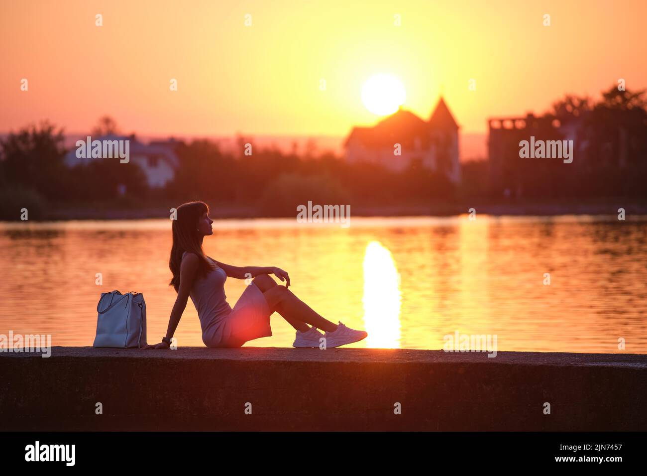 Lonely woman sitting on lake side on warm evening. Solitude and ...