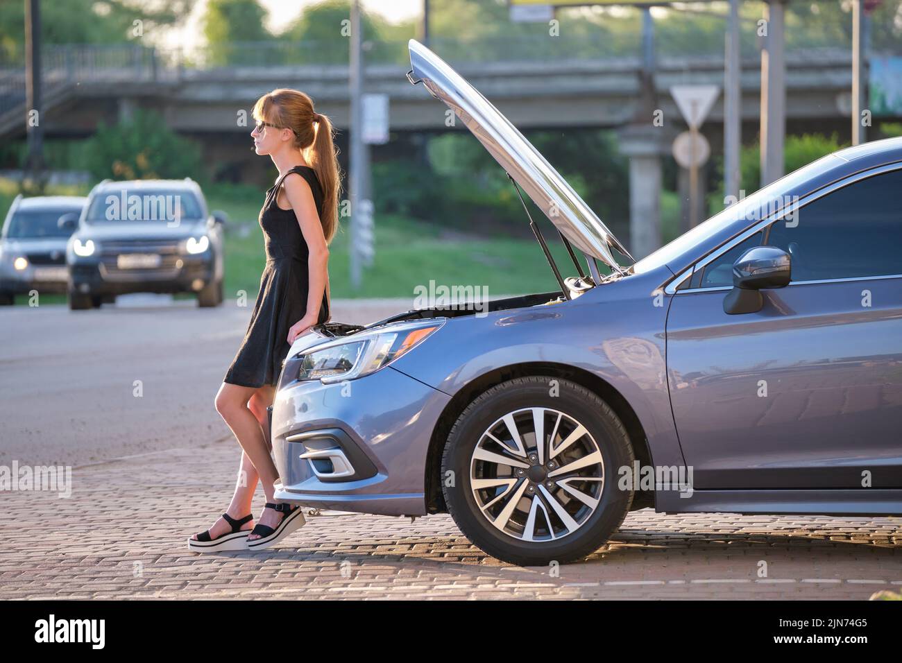 Sad female driver standing on a city street near her car with popped up ...