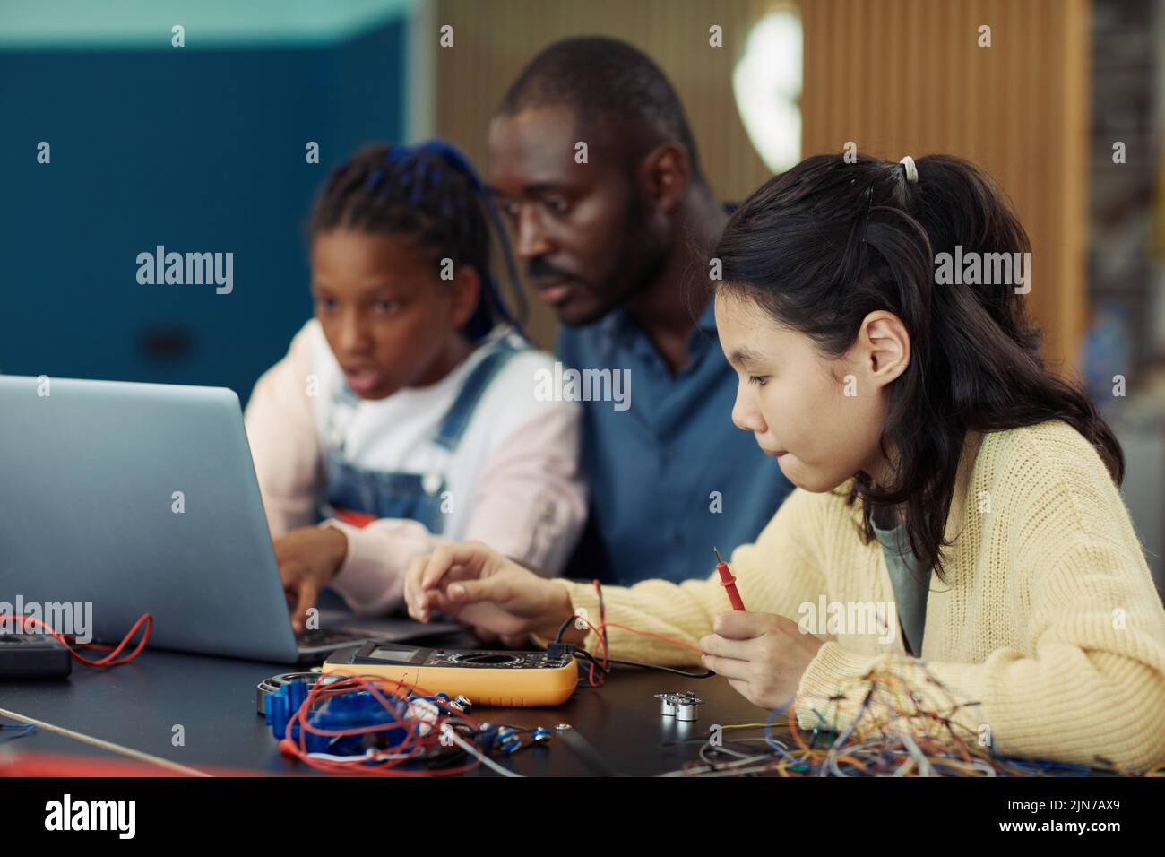 Side view portrait of Asian teenage girl building robot during engineering class in school with ...
