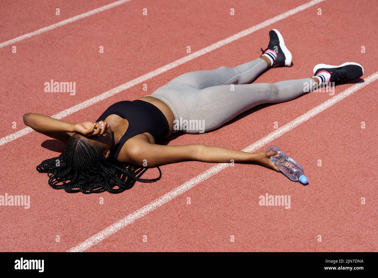 Powerless African American woman in sportswear lies on red track ...