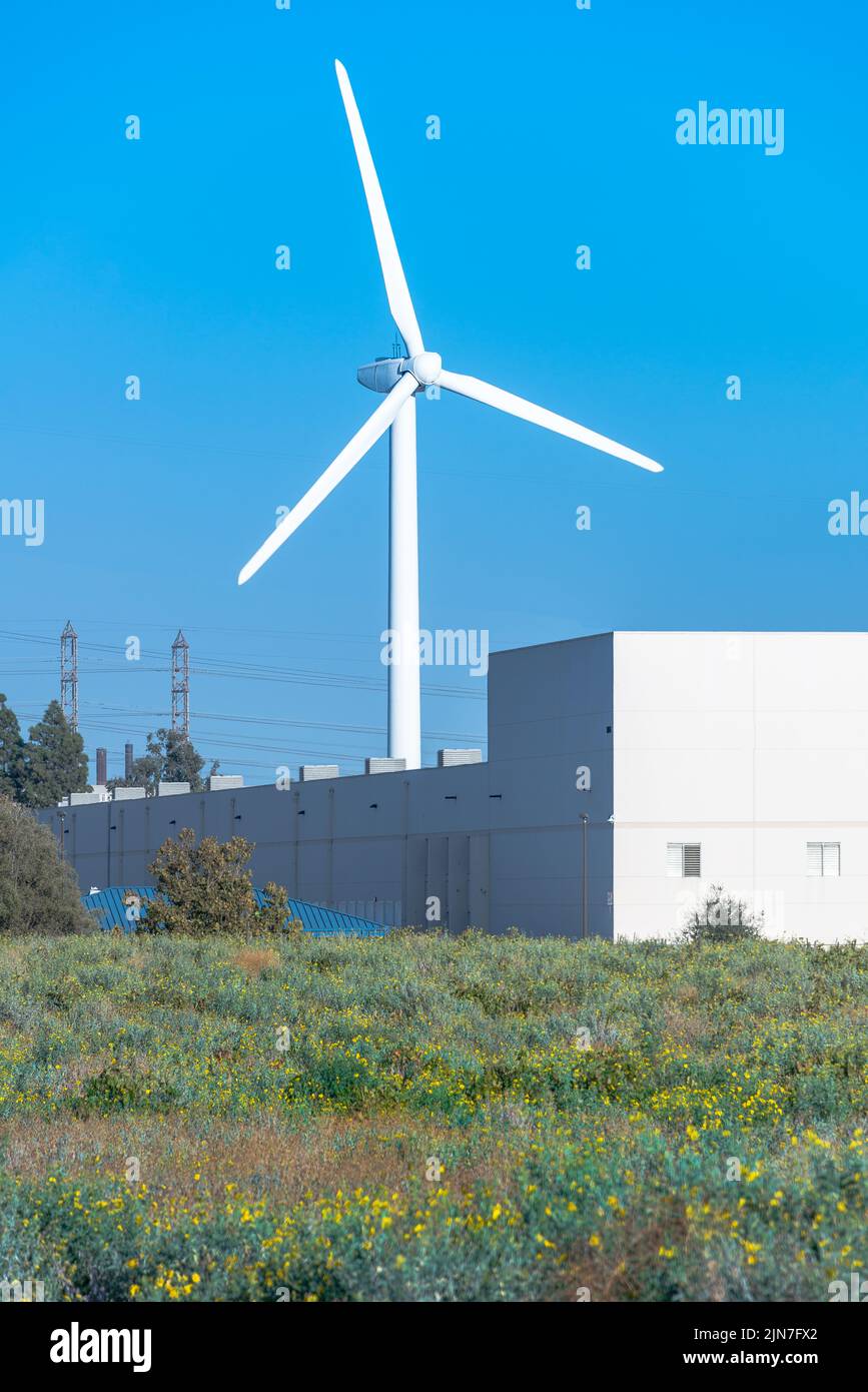 Wind turbine tower pictured beside plain white three-story building ...