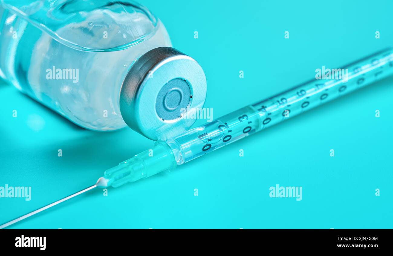 Glass vial with clear liquid and hypodermic syringe needle near, close ...