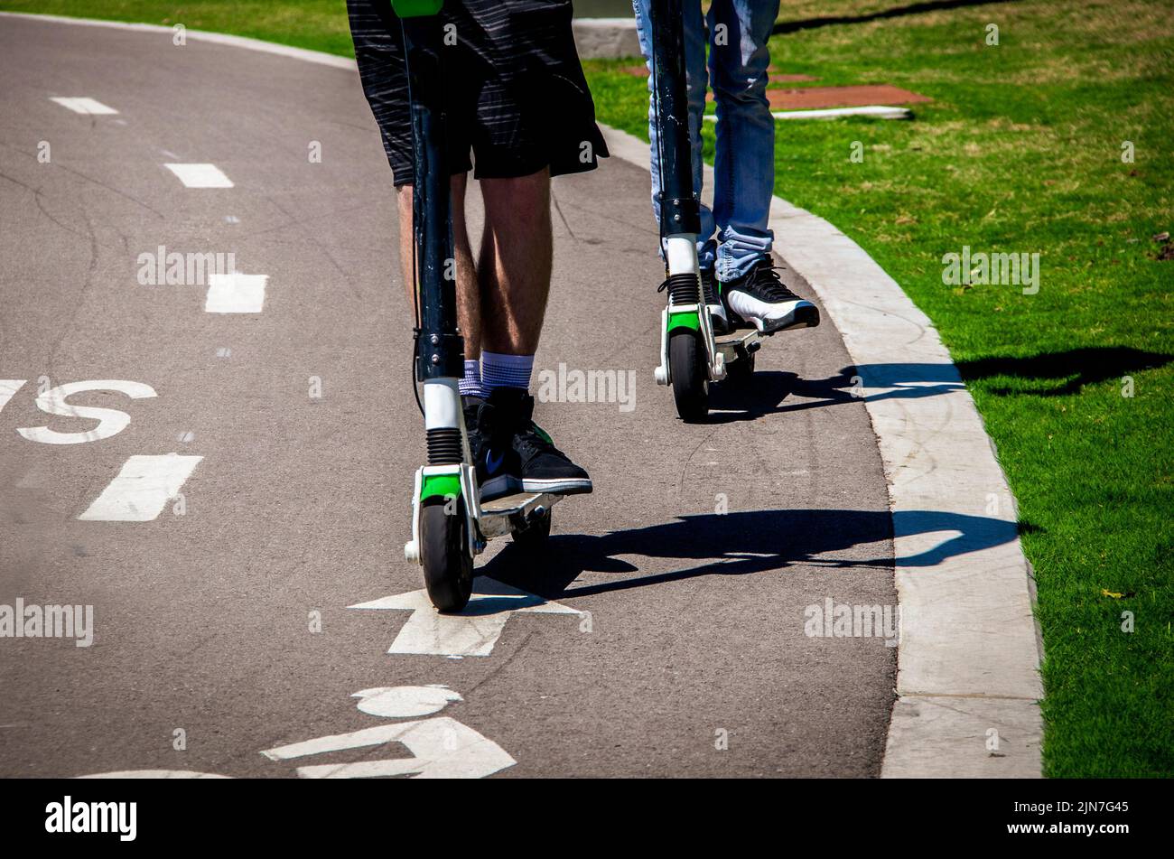 Two boys on motorized scooters - cropped to legs - on trail in park in ...