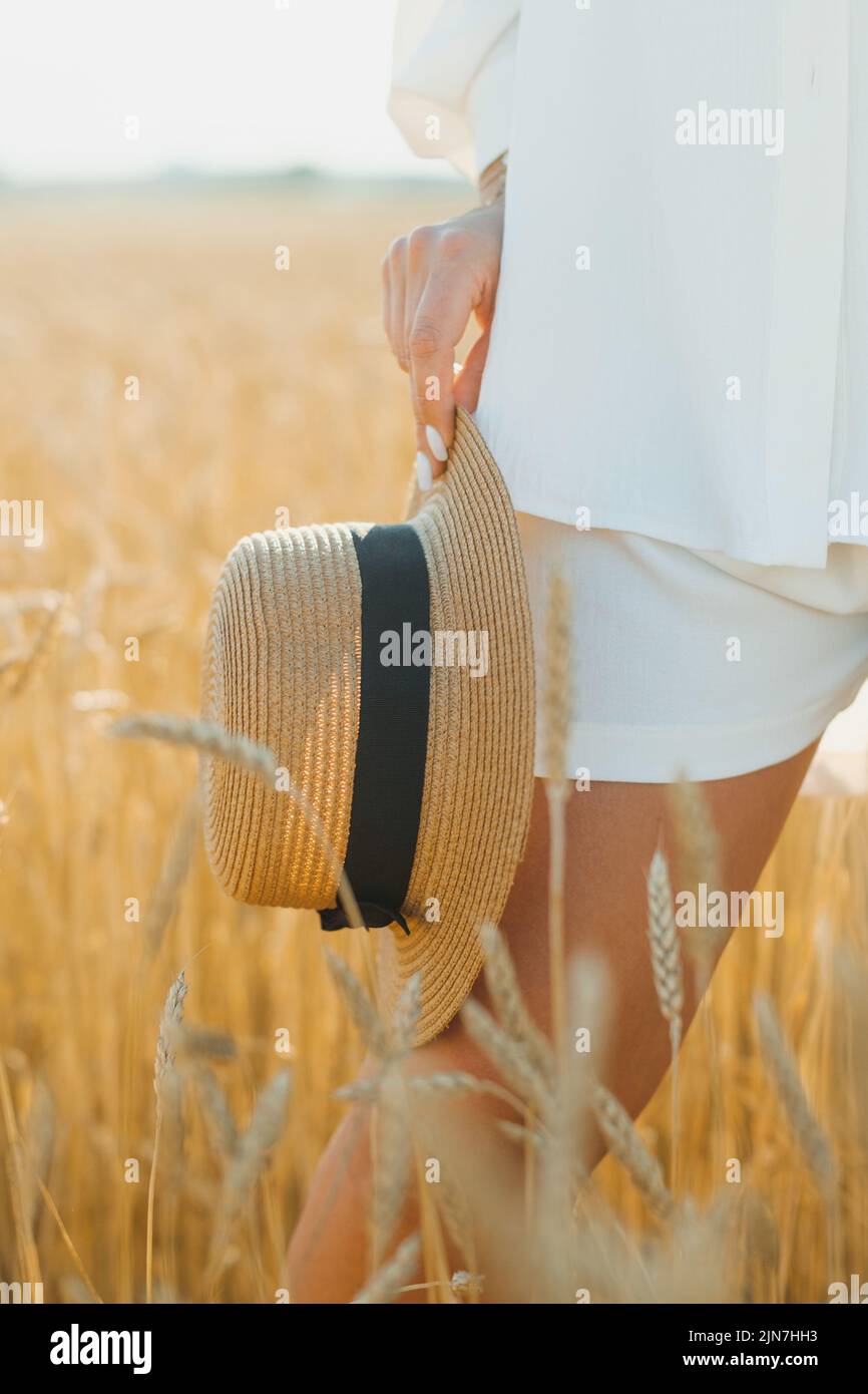 Closeup shot of female hand holding straw hat in a wheat field on a ...