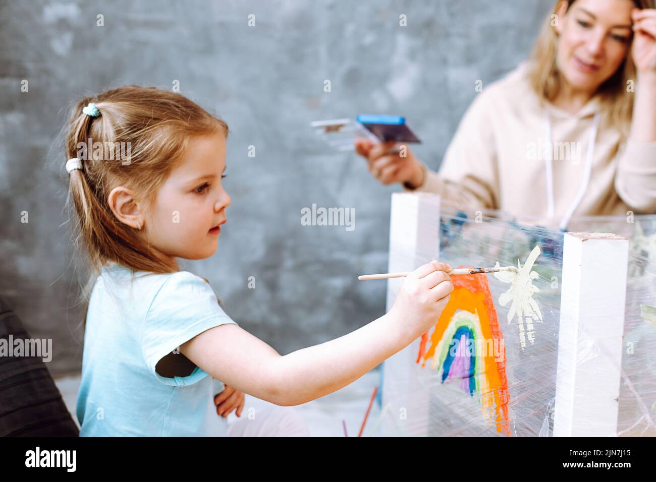 Portrait of busy little girl sitting on art lesson drawing with brush ...