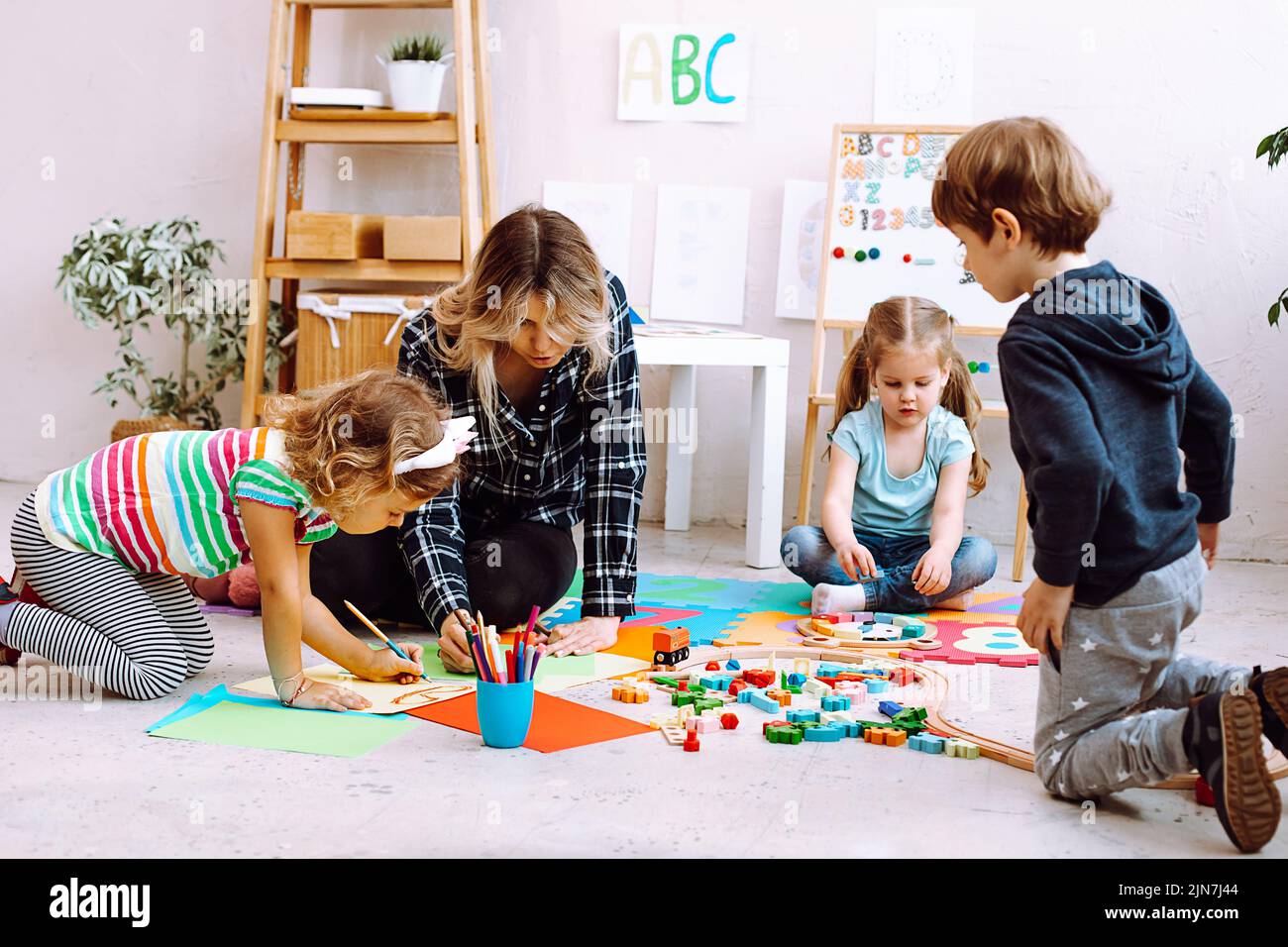 Young concentrated woman teacher sitting on floor with children ...