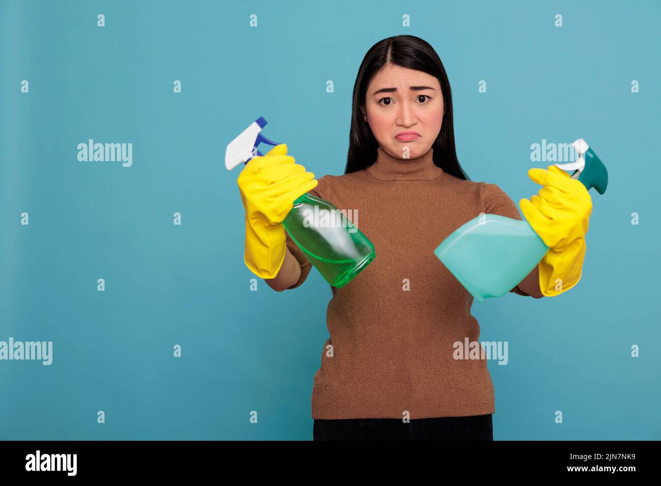 Sadly angry young asian woman holding two detergent spray in yellow ...