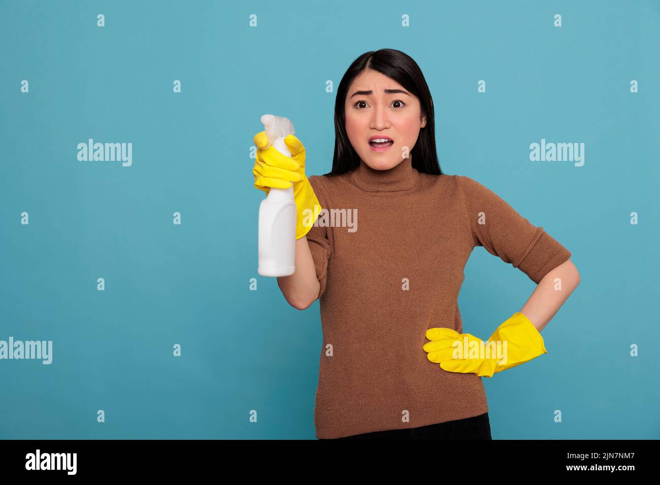 Shocked surprised asian housekeeper from chores holding spray in yellow ...