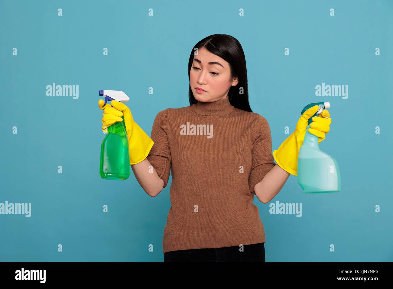 Portrait of pretty sad asian woman holding two detergent sprayers in ...