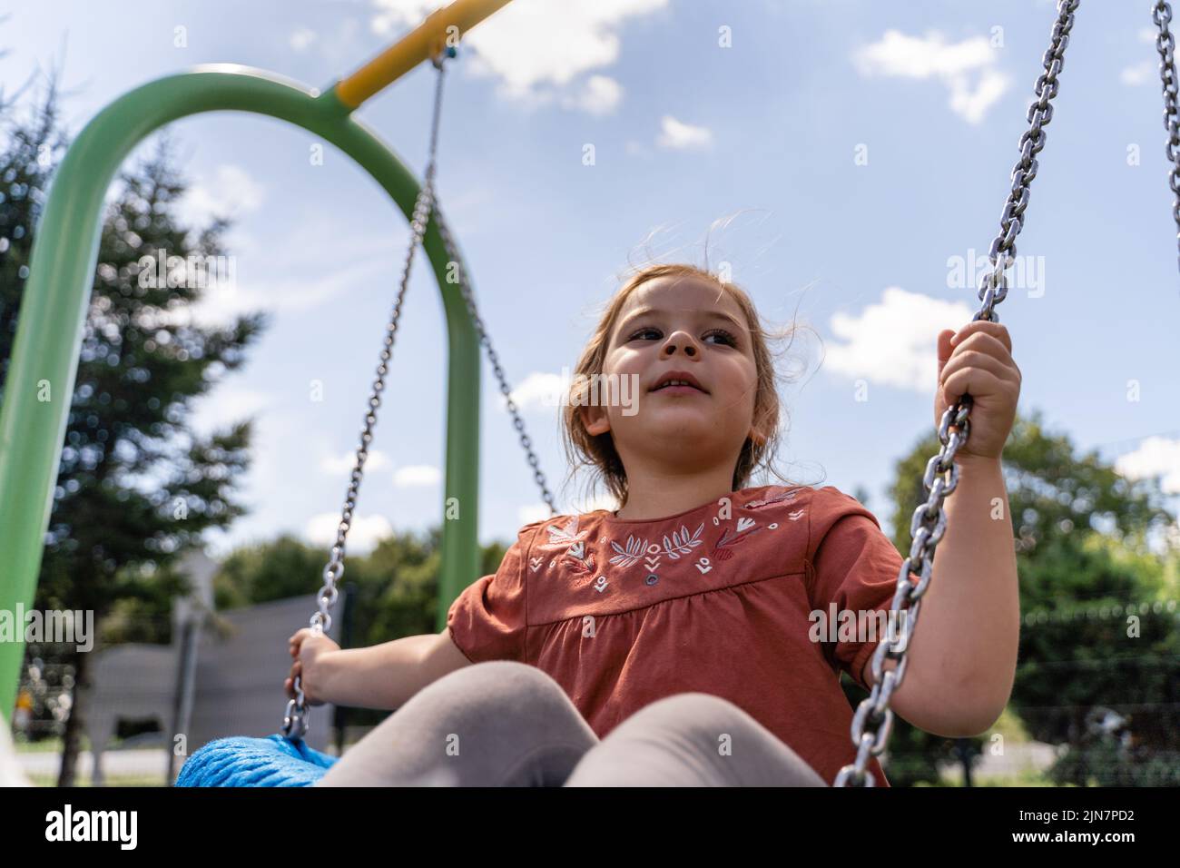 Preschooler caucasian girl swinging on rope net swing on playground ...