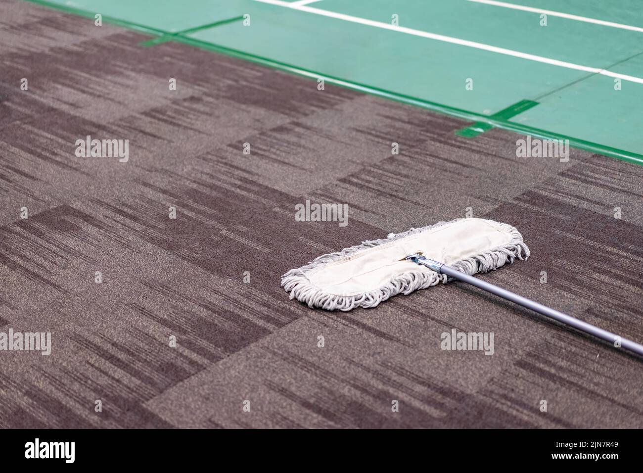 A white badminton court mop is placed in front of a black chair located ...