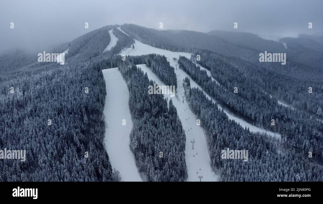 An aerial shot of skiing slopes lined with dense forests and a ropeway ...