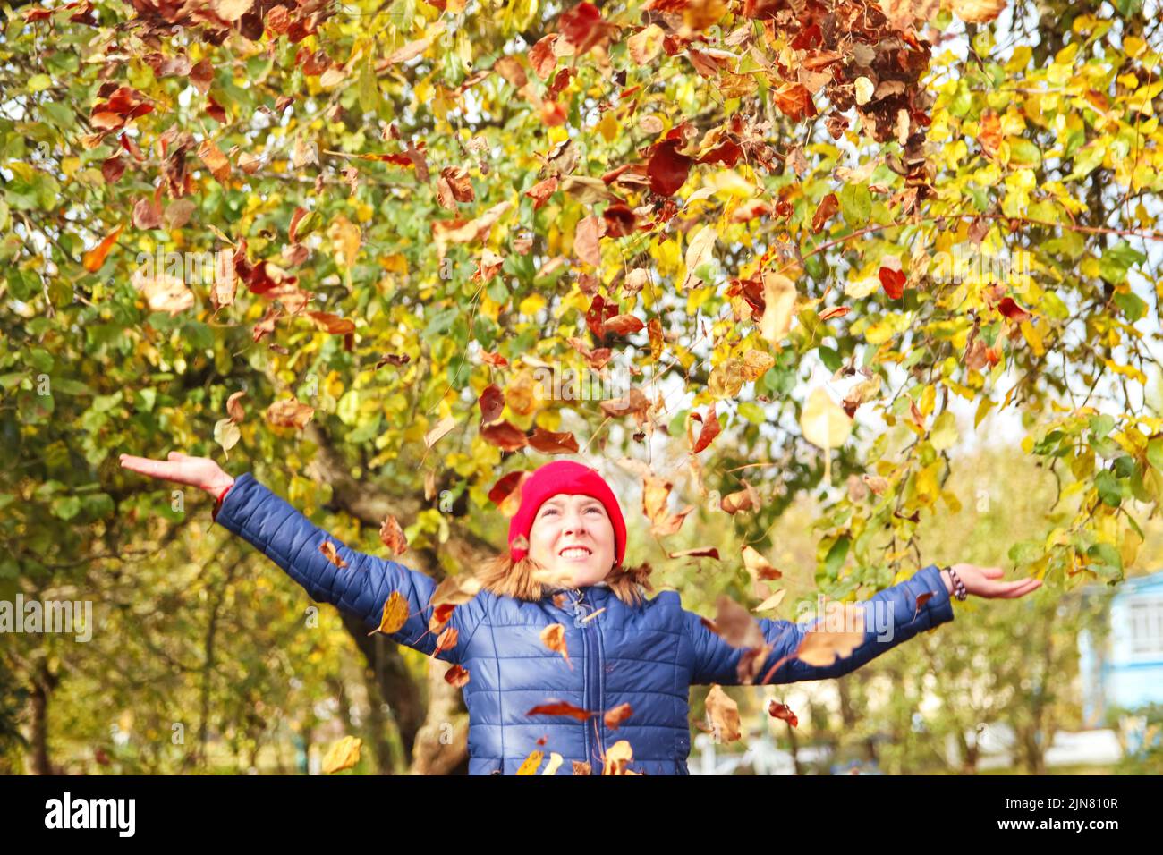 Defocus autumn people. Teen girl raising hand and throwing leaves. Many ...