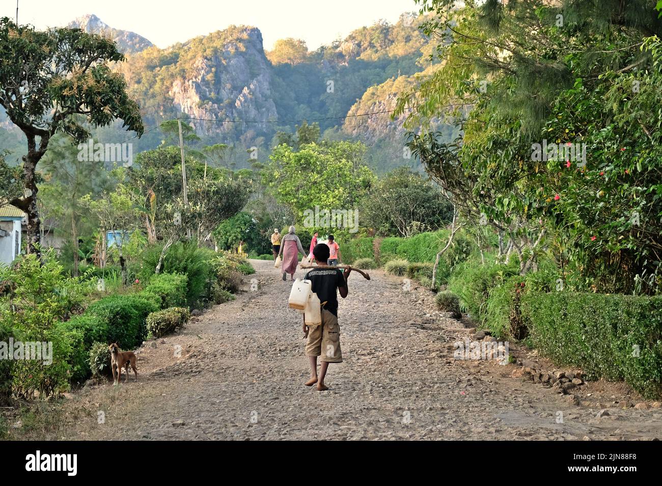 A young man carrying jerry cans as he is walking on a rural road to ...