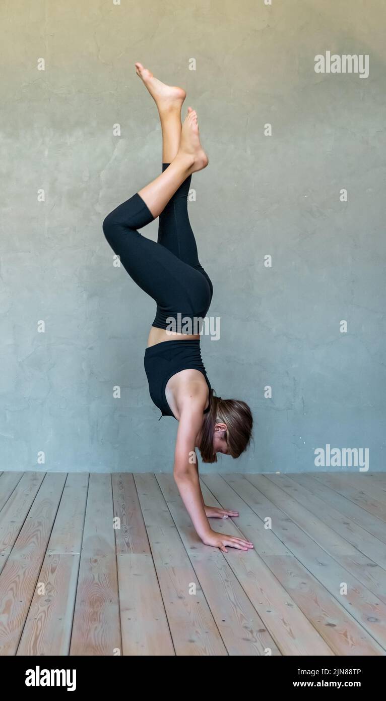 A girl practices yoga doing a headstand pose on the floor in a room in ...