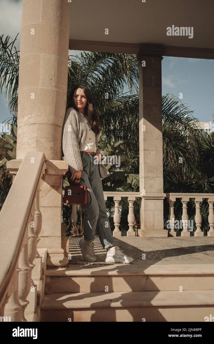 Woman stand near old building with columns and tropical plants in ...