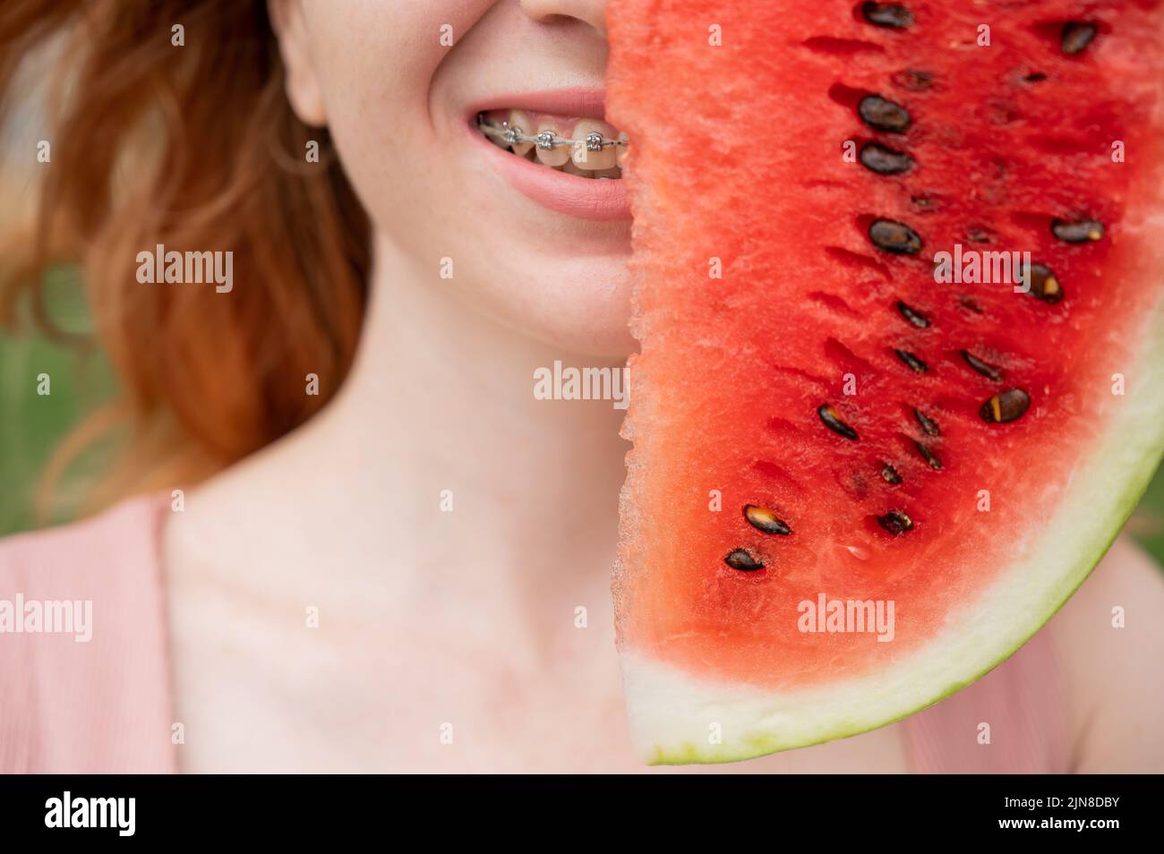 Beautiful red-haired woman smiling with braces on her teeth covers half ...