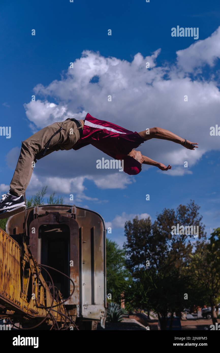 Hispanic man dressed in red with urban clothing doing a somersault with ...