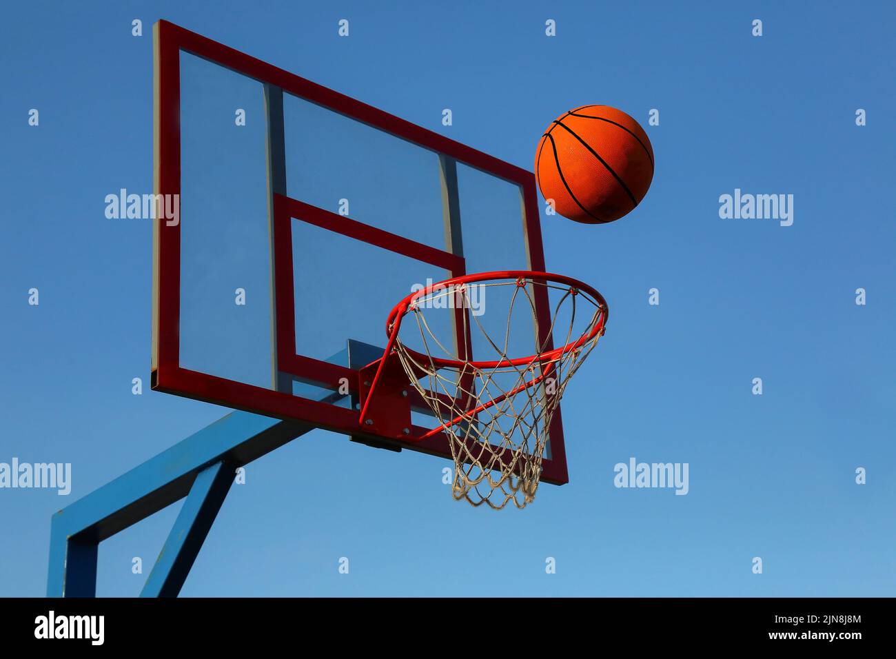 A basketball against the blue sky is flying into the basket. Outdoor ...