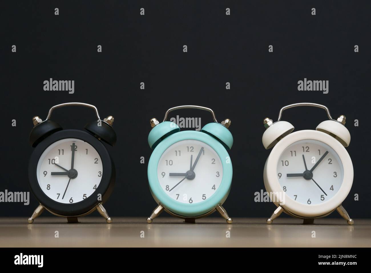 Three small alarm clocks black blue and white show nine o'clock, stand ...