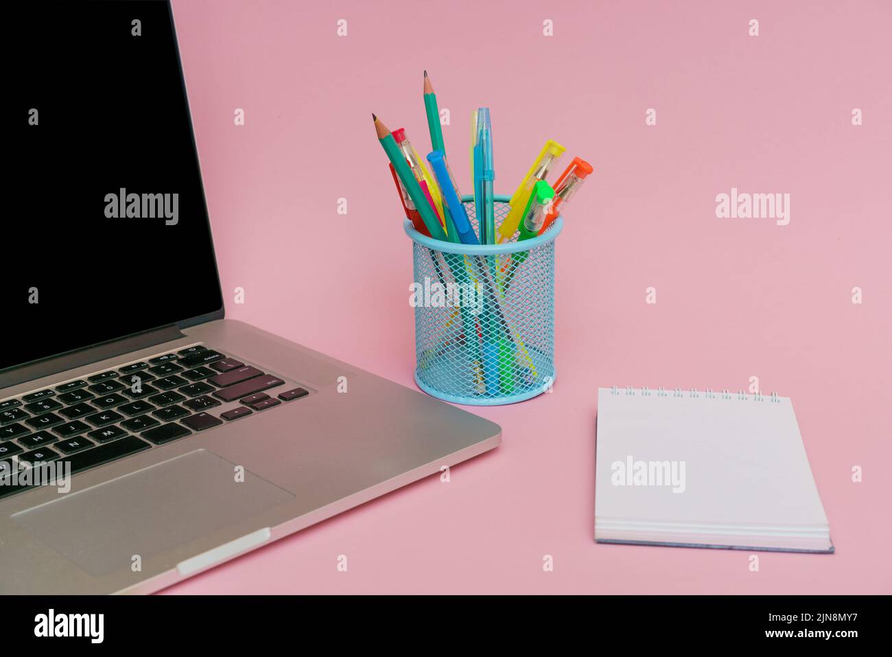 Laptop pens and colored pencils in blue stand and white stickers on ...