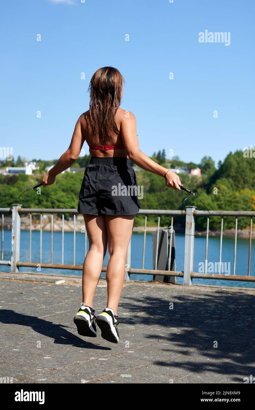 A vertical shot of young female wearing sporty cloth and jumping rope ...