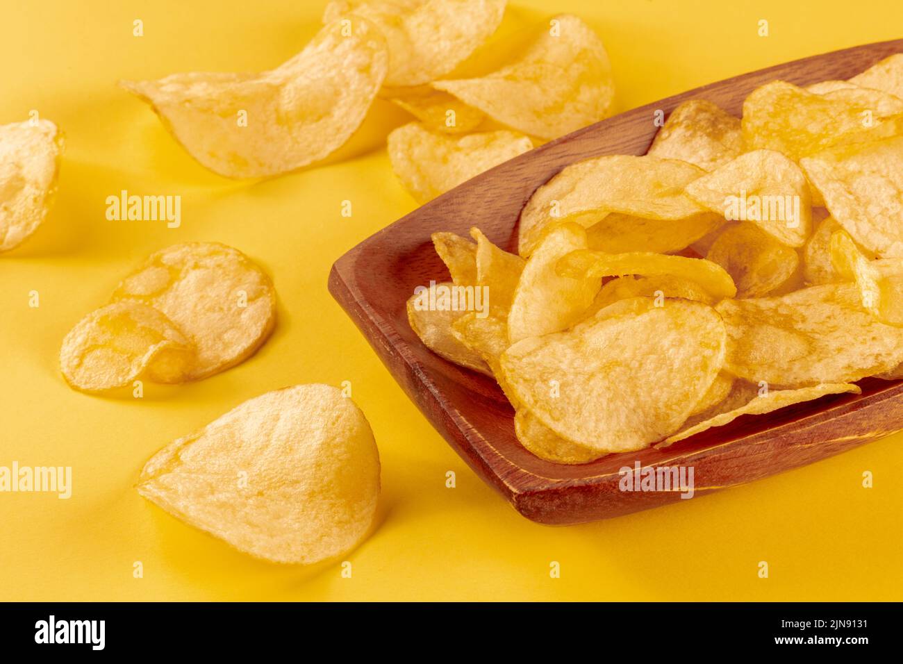 Potato chips or crisps in a bowl and scattered on a yellow background ...